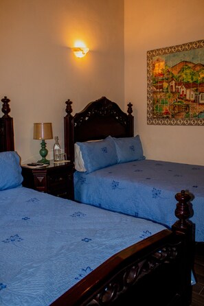 Quarto com duas camas, mesa de cabeceira com abajur, garrafa e pintura na parede.