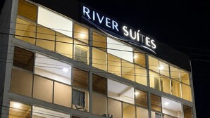 Um hotel com vários andares, com o nome 'River Suites' iluminado na fachada.