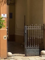 Uma entrada protegida por portão, com placa, planta em vaso e um pilar de pedra.