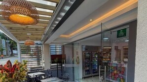 Um café ao ar livre com mesas e cadeiras, entrada por uma porta de vidro e vista para uma loja.