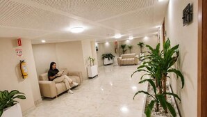 Um saguão de hotel com área de estar, balcão de recepção e plantas em vasos.