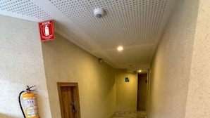 Corredor com extintor, porta e teto com padrão perfurado.