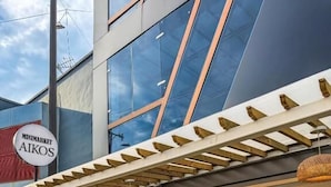 Um edifício com fachada, um letreiro indicando 'MININARKET AIKOS' e uma área externa coberta com plantas.