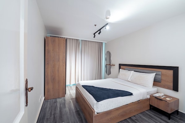 Quarto de hotel moderno com cama de madeira, mesa de cabeceira, guarda-roupa e luminária no teto.