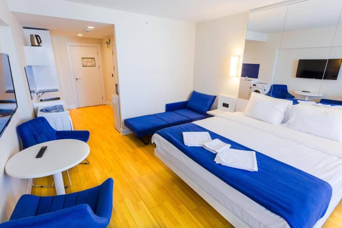 Quarto de hotel com uma cama grande, uma secretária pequena com cadeira, um sofá e uma televisão.