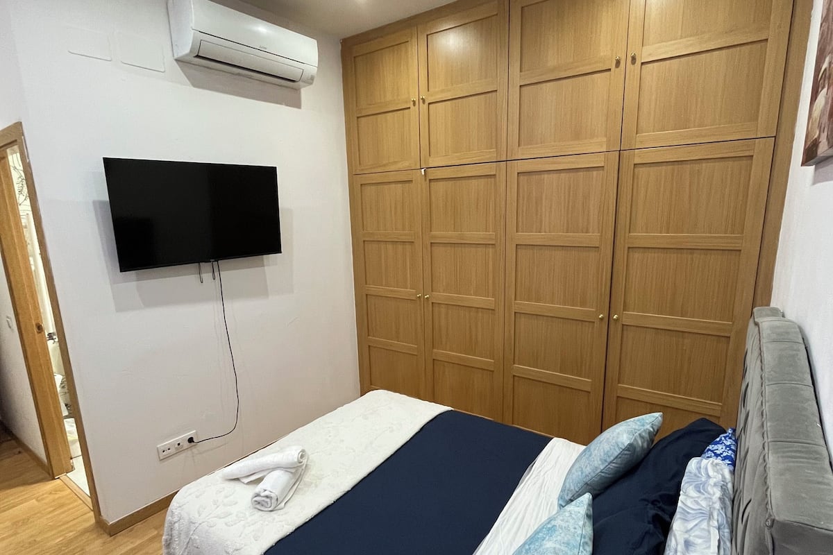 Quarto com cama, televisão, guarda-roupa de madeira e ar condicionado.