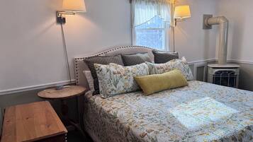 Quarto com cama, luminárias de cabeceira, uma mesa redonda e uma janela com cortinas.