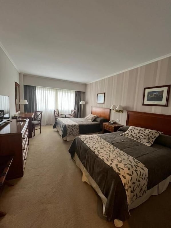 Quarto de hotel com duas camas, uma escrivaninha, uma cadeira e uma televisão.
