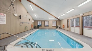 Piscina interna com placa de 'NÃO MERGULHAR', boias salva-vidas e aviso de salva-vidas.