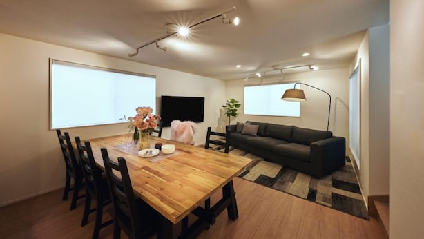 Uma sala de estar moderna com uma mesa de jantar de madeira, sofá escuro e uma janela grande.
