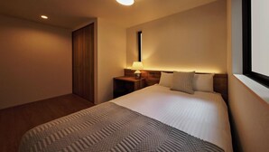 Quarto de hotel com cama, mesa de cabeceira, abajur e janela.