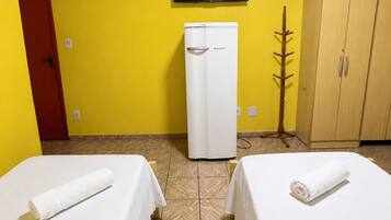 Quarto com duas camas, televisão, ventoinha, frigorífico e um cabideiro de madeira.