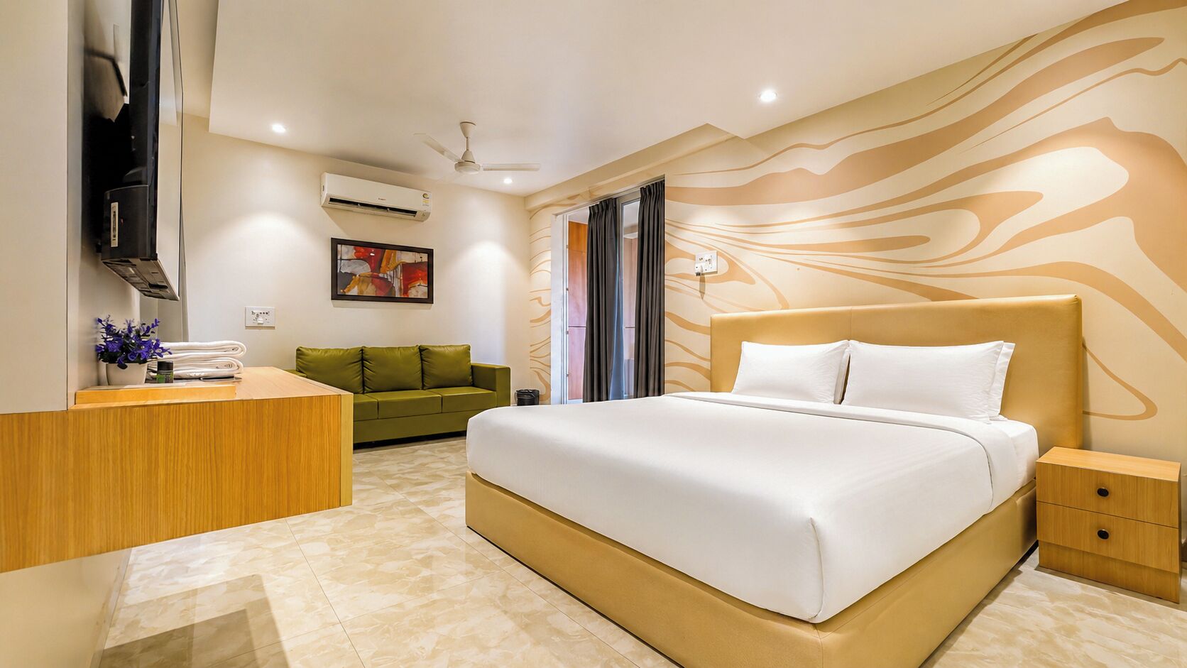 Quarto de hotel com cama, escrivaninha, sofá verde e televisão.
