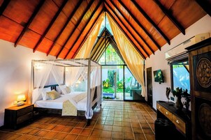 Quarto com cama de dossel, mesa de cabeceira, penteadeira e vista para o exterior.
