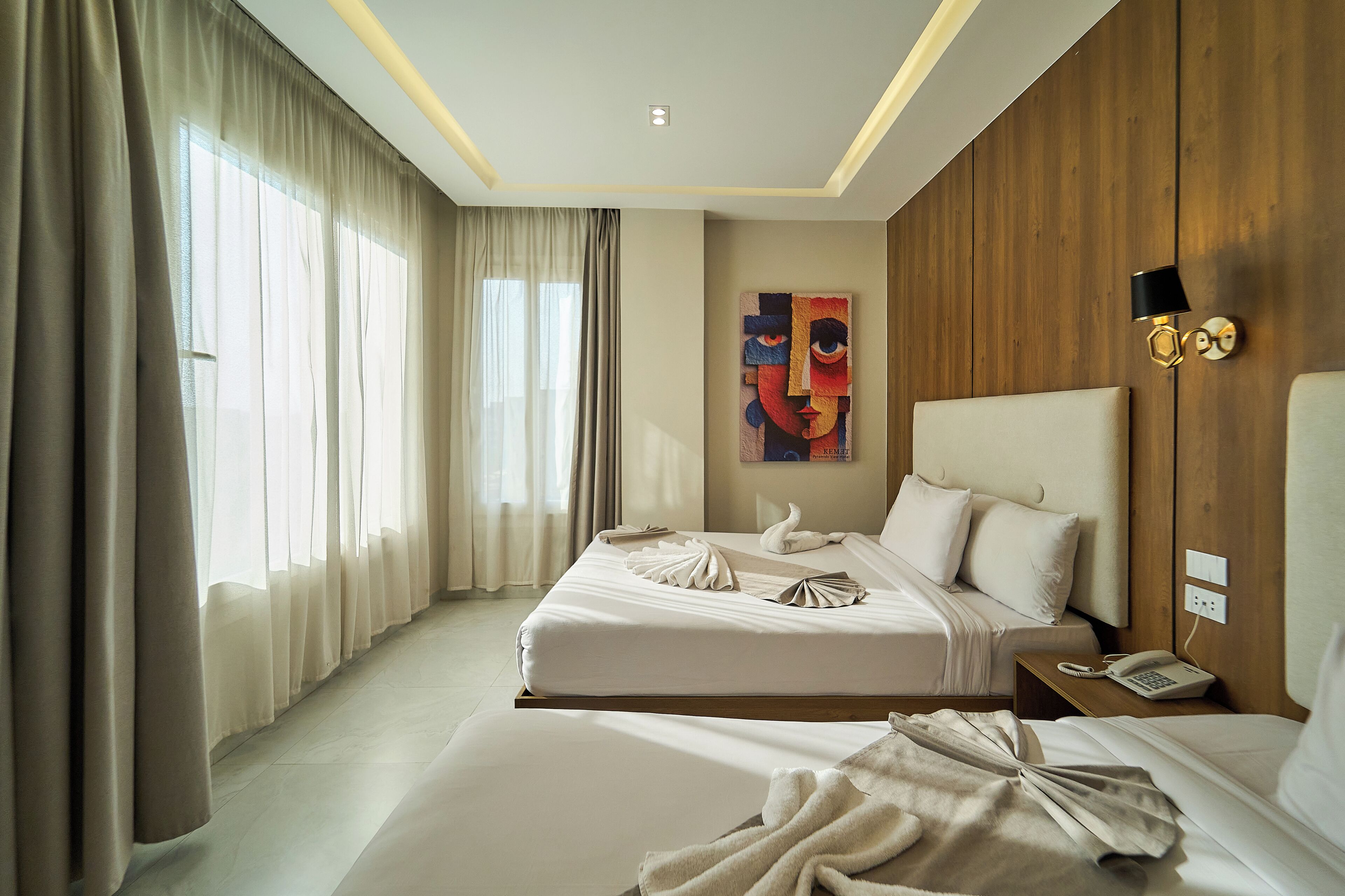 Quarto de hotel com duas camas, um quadro na parede, uma luminária e um telefone na mesa de cabeceira.