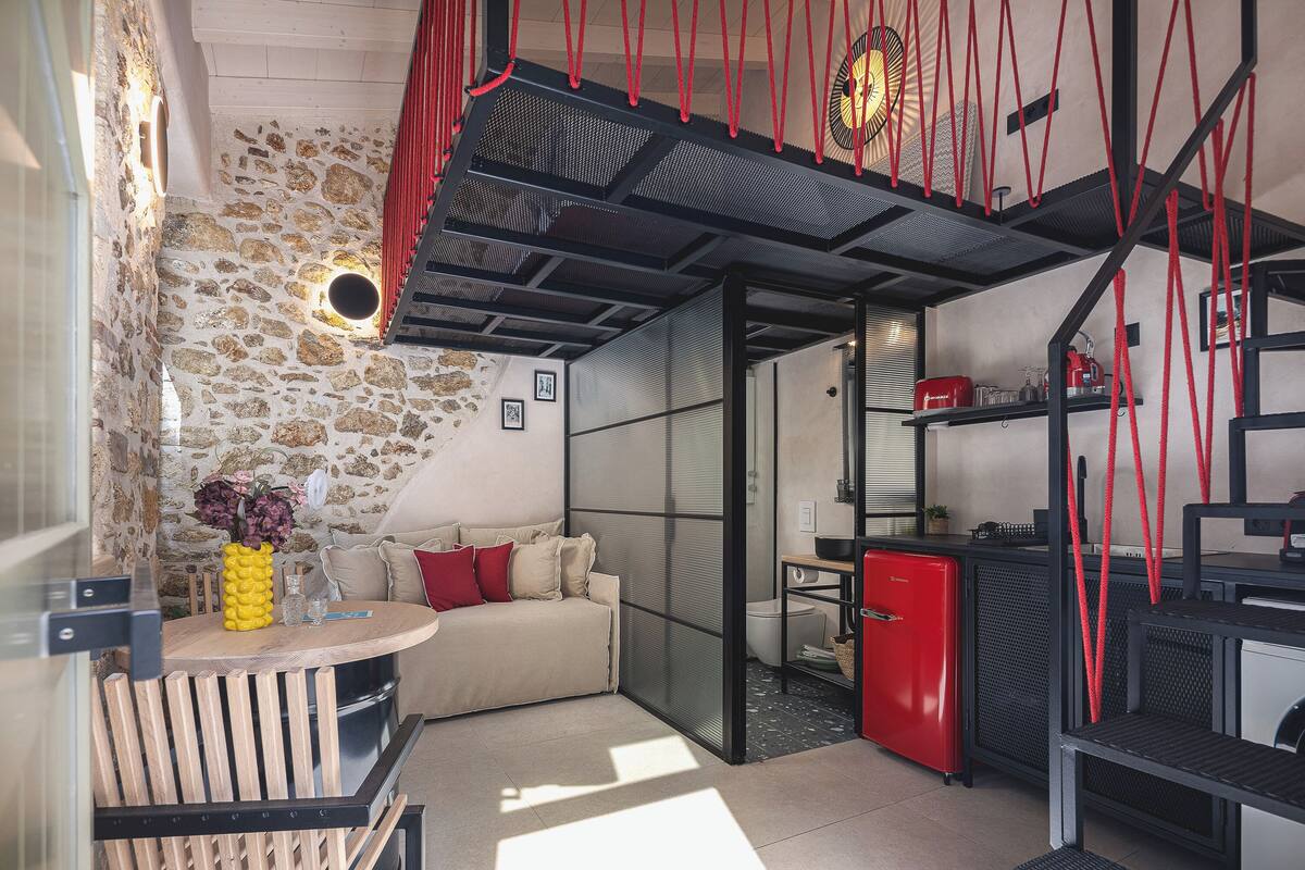 Um espaço de estar compacto com parede de pedra, um sofá, uma mesinha, um armário vermelho e uma área de cozinha.