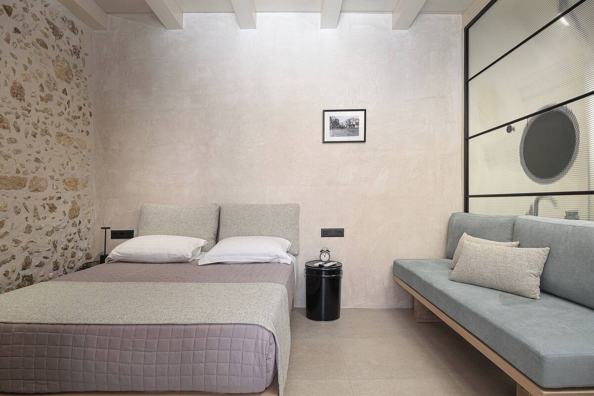 Quarto com uma cama, um sofá, uma lixeira e um quadro na parede.