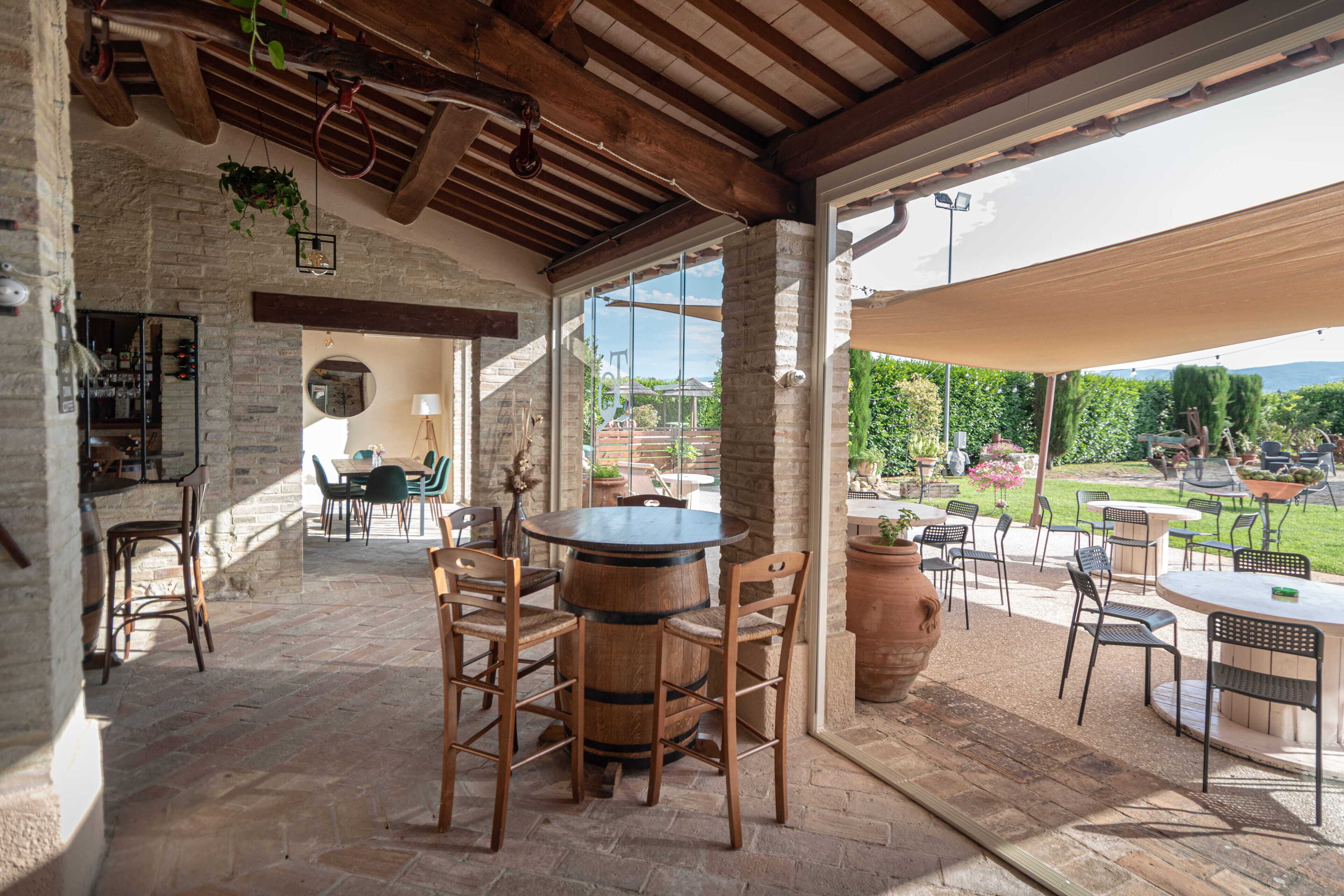 Um pátio externo com uma mesa redonda de madeira e cadeiras, um vaso grande e vista para um jardim.