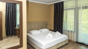 Quarto com uma cama grande, mesa de cabeceira, espelho e janela com cortinas.