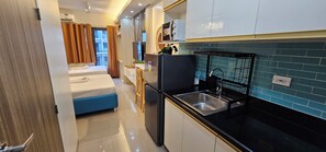 Quarto de hotel compacto com cozinha americana, uma cama, um pequeno espaço de refeições e vista para um edifício pela janela.
