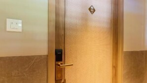 Uma porta de madeira com painel texturizado e um pequeno emblema, em um corredor com piso de mármore.