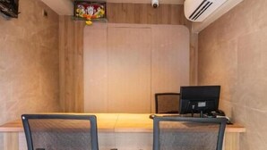 Um quarto com duas cadeiras de escritório pretas, uma escrivaninha de madeira, um computador e um aparelho de ar condicionado.