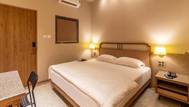 Quarto de hotel com cama, luminárias de cabeceira, escrivaninha, cadeira e ar condicionado.