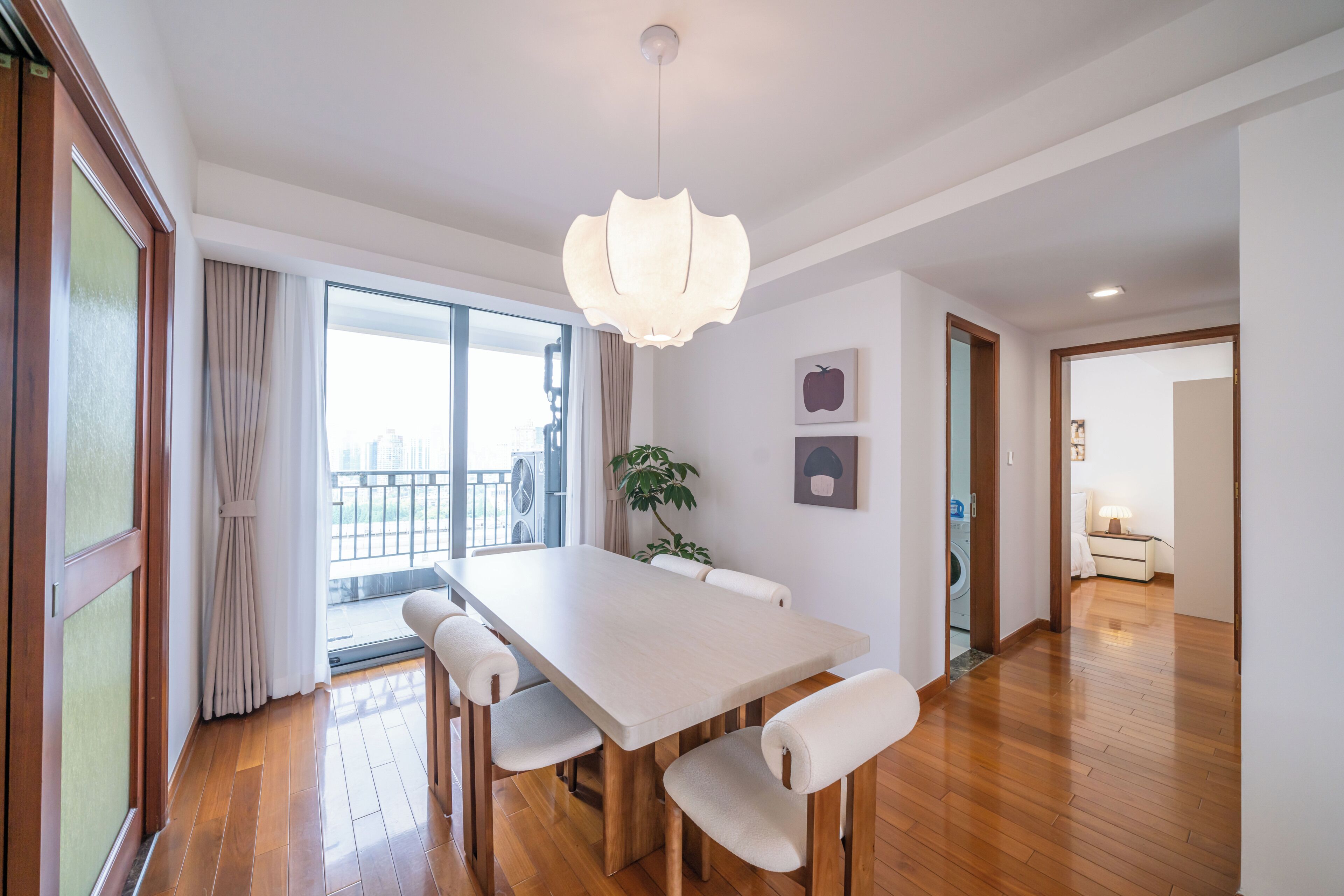 Uma sala de jantar com uma mesa grande, cadeiras, um lustre e vista através de uma porta de vidro.