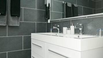 Um banheiro moderno com azulejos escuros, um lavatório branco, um espelho e um porta-toalhas.
