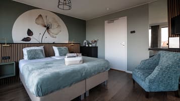 Um quarto com cama, poltrona, cómoda, televisão fixada na parede e uma grande obra de arte floral.
