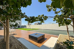 Uma área externa moderna com deck de madeira, um fire pit quadrado e uma piscina.