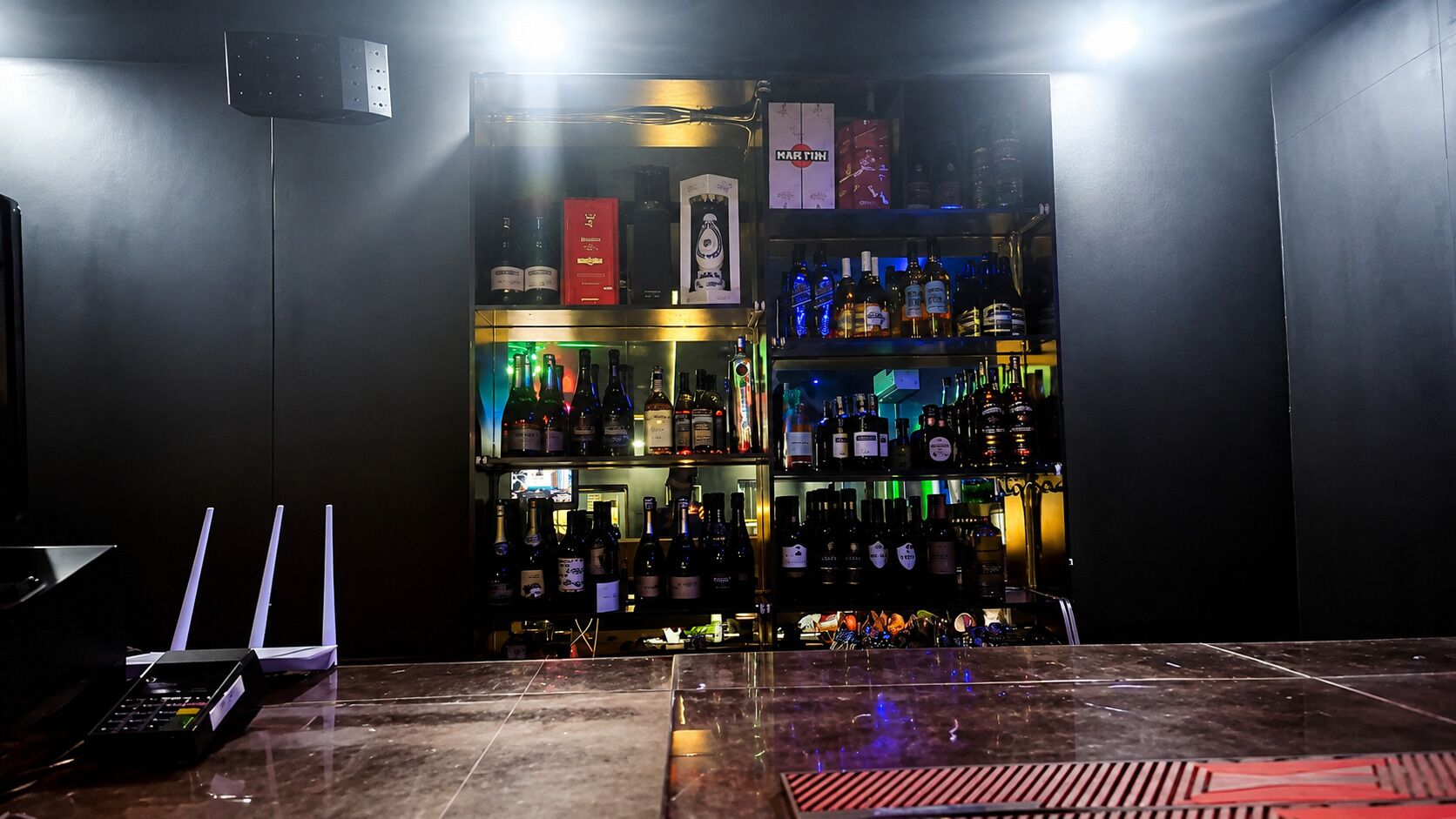 Uma área de bar com várias prateleiras de garrafas, um caixa registradora e uma única mesa.