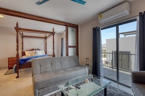 Quarto com cama de dossel, sofá cinza, mesa de centro de vidro e varanda com vista.