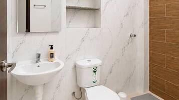 Casa de banho com lavatório, sanita e chuveiro, tudo em branco.