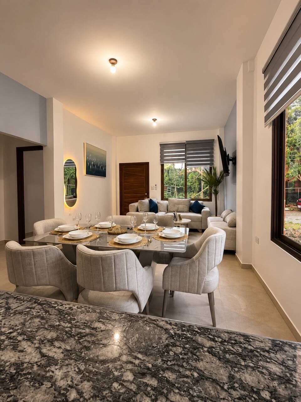 Uma zona de refeições moderna com uma mesa de mármore, cadeiras brancas e um sofá.