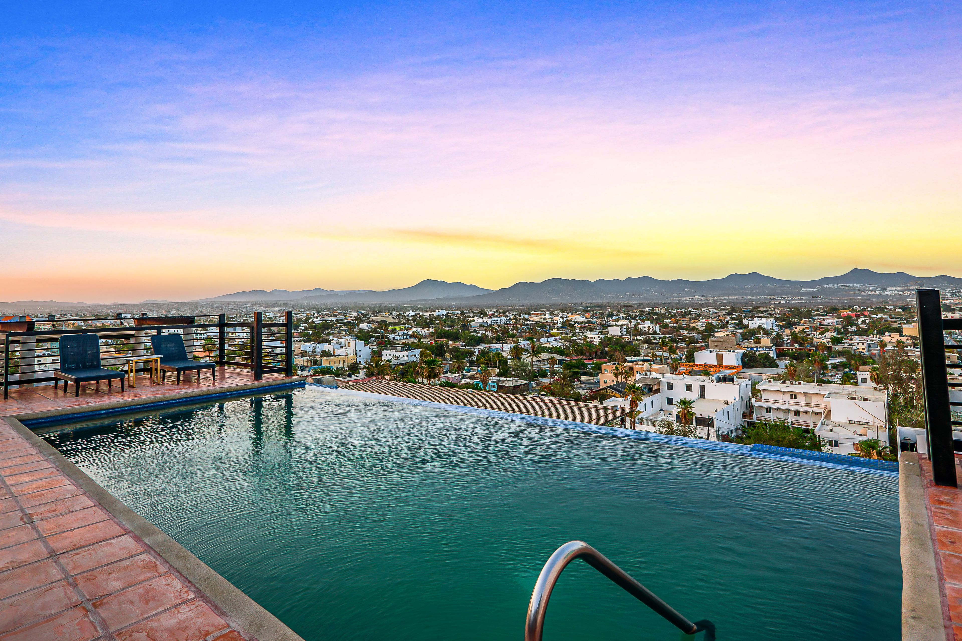 Uma piscina infinita com vista para um horizonte urbano e montanhas ao longe.