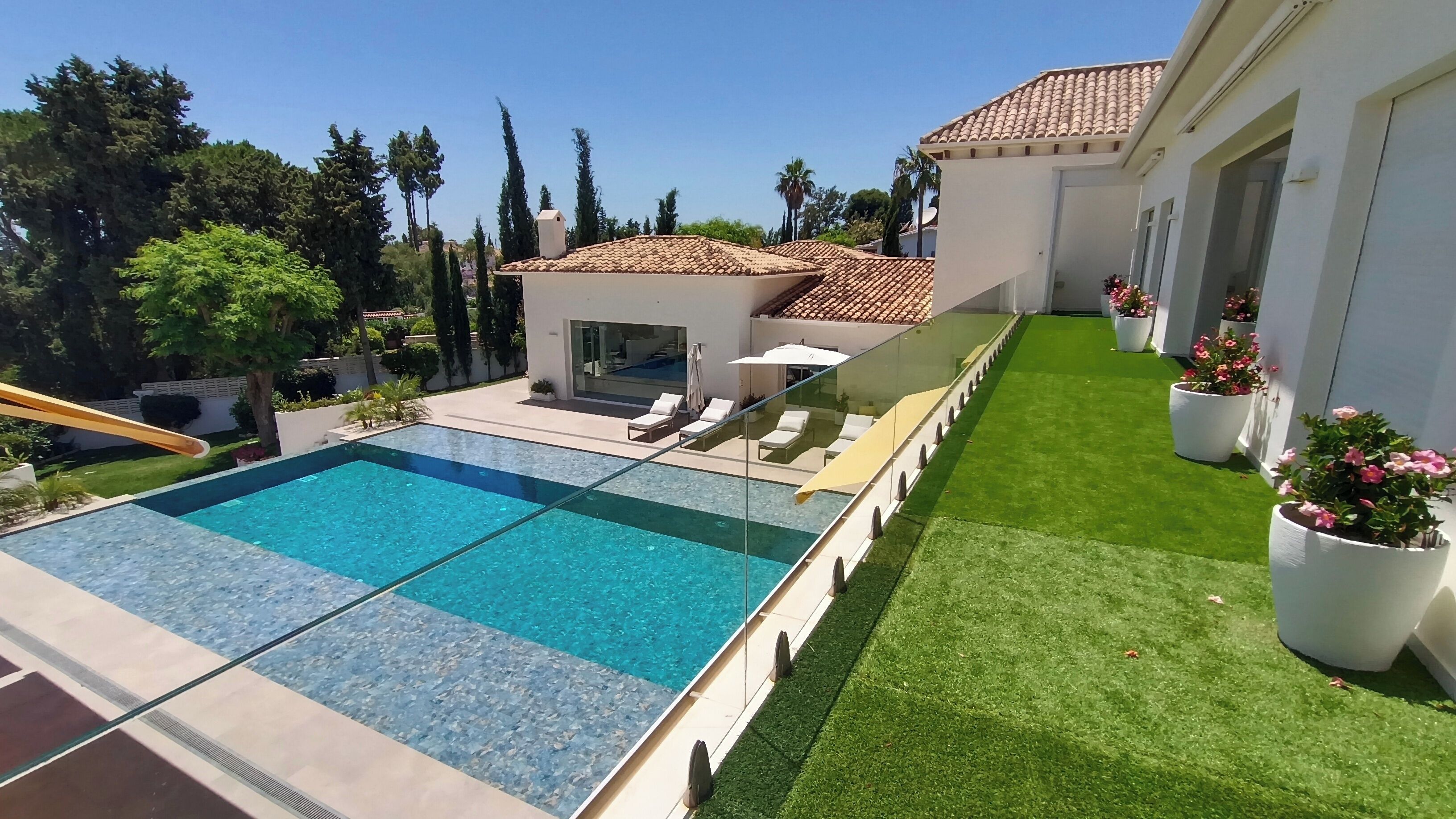 Piscina com borda de vidro, área de estar coberta e gramado bem cuidado.
