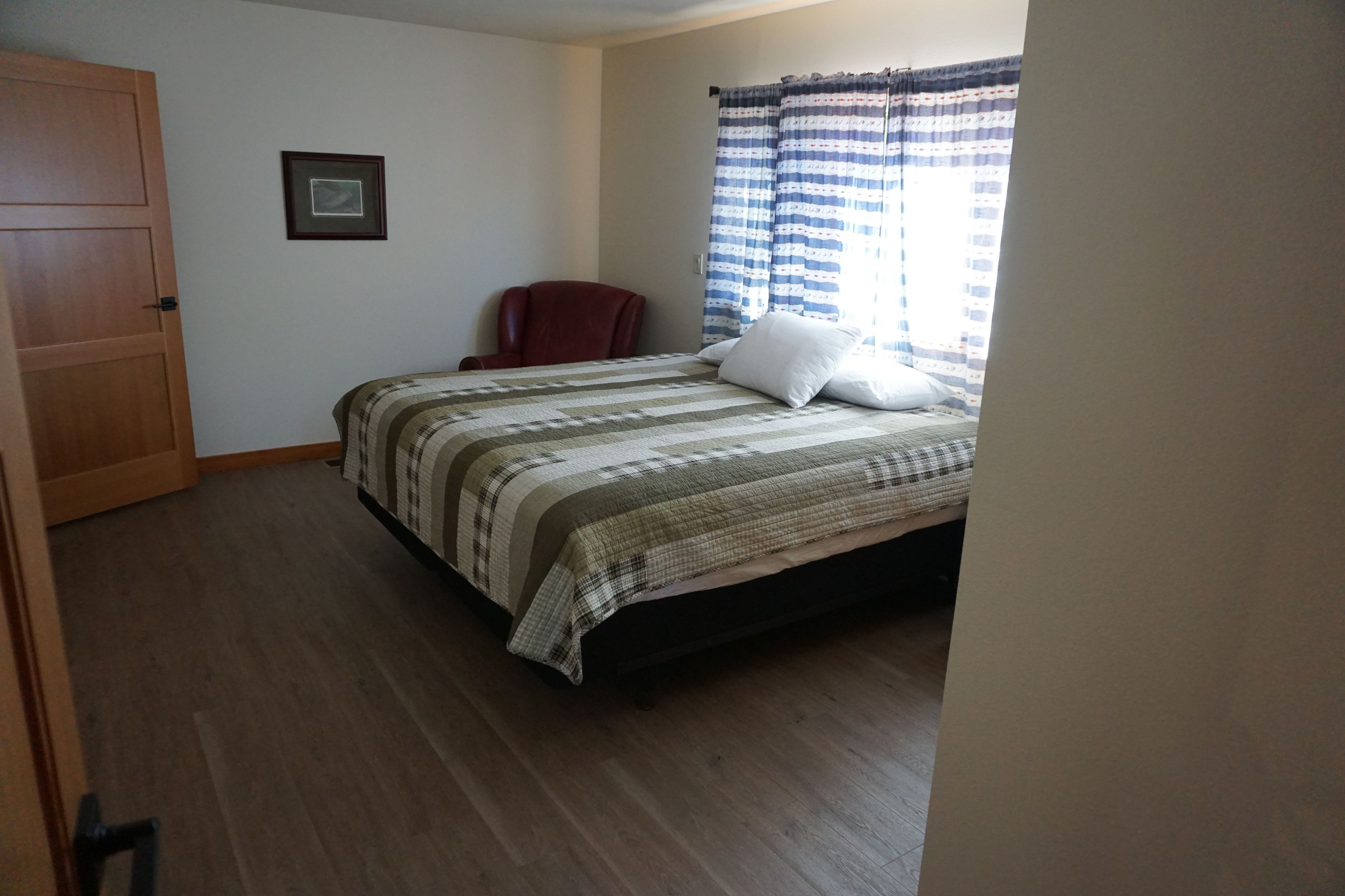 Quarto com cama, cadeira, porta e janela com cortinas.