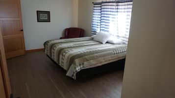 Quarto com cama, cadeira, porta e janela com cortinas.
