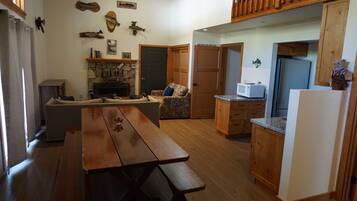 Uma sala de estar acolhedora com um banco de madeira, uma lareira de pedra e uma mesa de jantar.