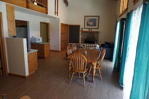 Ampla sala de estar com mesa de jantar de madeira e cadeiras, cozinha equipada com micro-ondas e lareira.