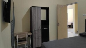 Quarto com cama, guarda-roupa, escrivaninha e televisão.
