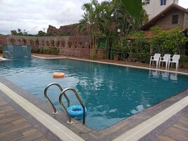 Piscina com plataforma de mergulho, espreguiçadeiras e um muro de pedra com plantas.