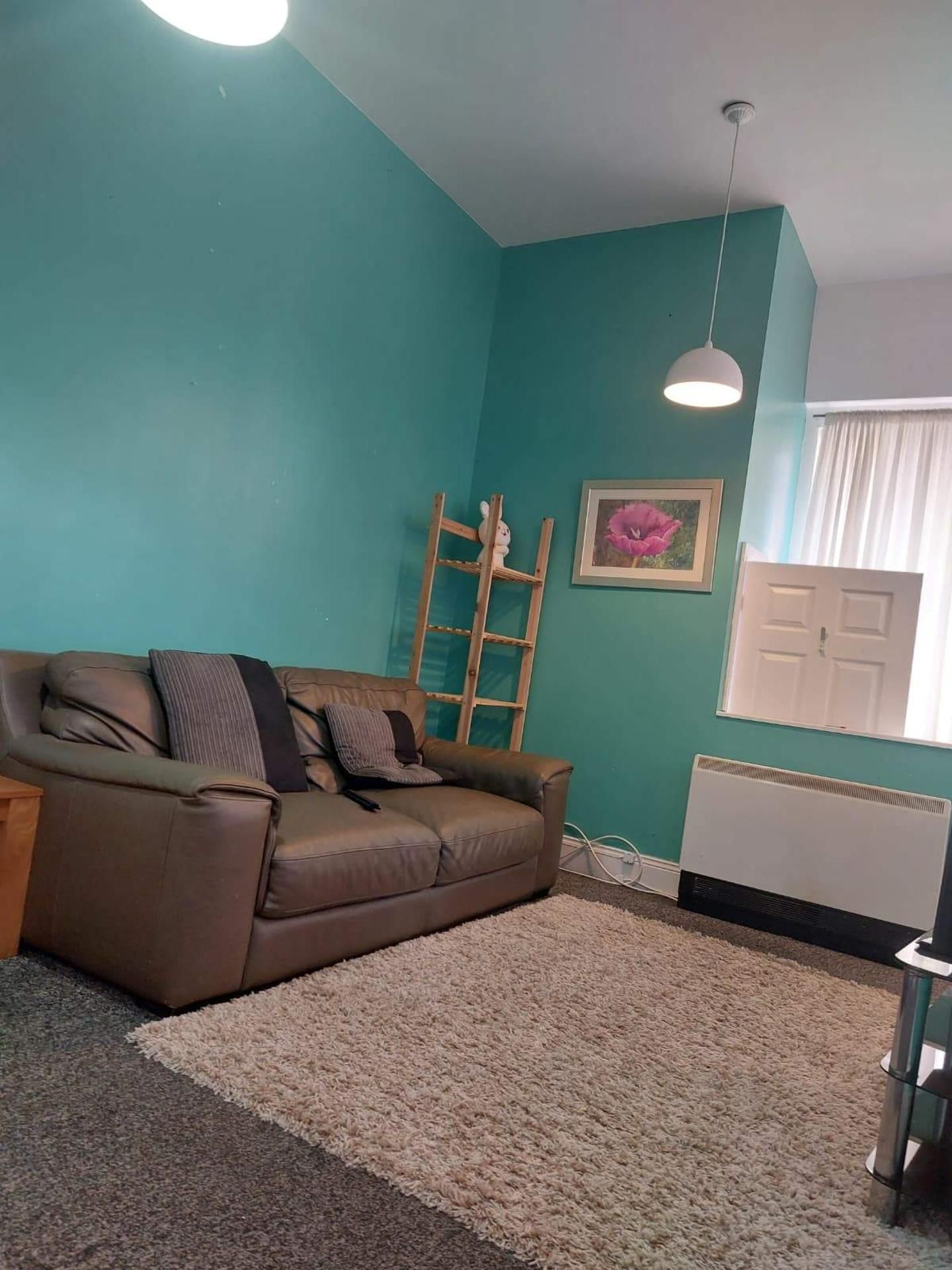 Sala de estar com paredes verde-água, um sofá marrom, um radiador branco e uma janela com cortinas brancas.