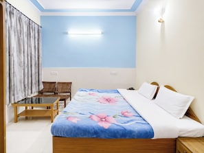 Quarto com cama, duas cadeiras de madeira, uma mesa pequena e luminária na parede.