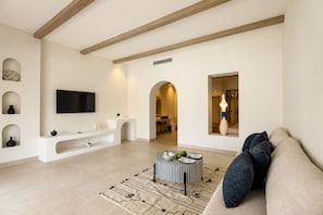 Uma sala de estar moderna com uma televisão de tela plana, um móvel branco para aparelhos eletrônicos, um tapete estampado e um sofá com almofadas.