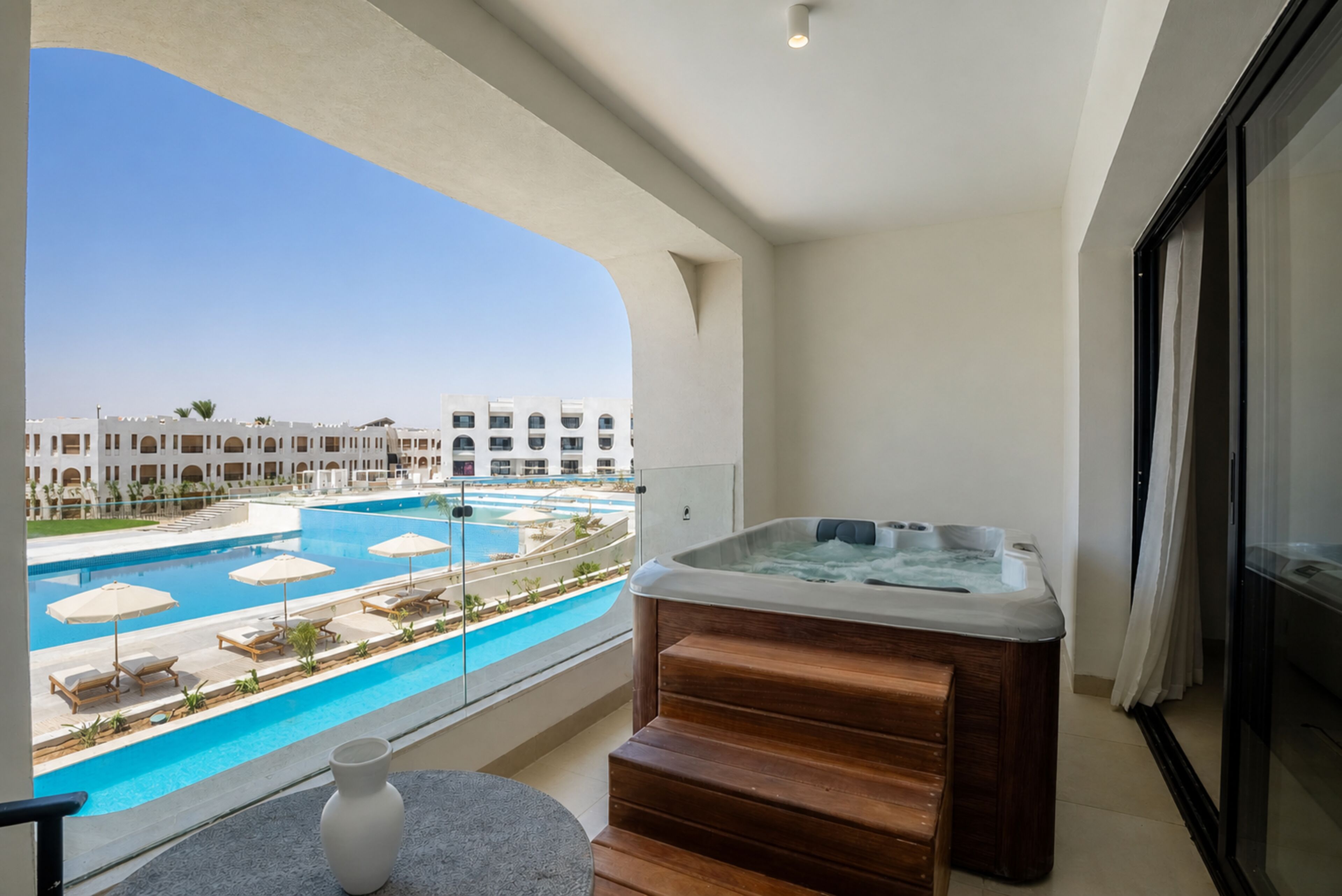 Uma varanda com banheira de hidromassagem, piscina e vista para um complexo hoteleiro.