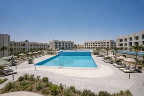 Uma área de piscina em resort, com várias piscinas, espreguiçadeiras e palmeiras.