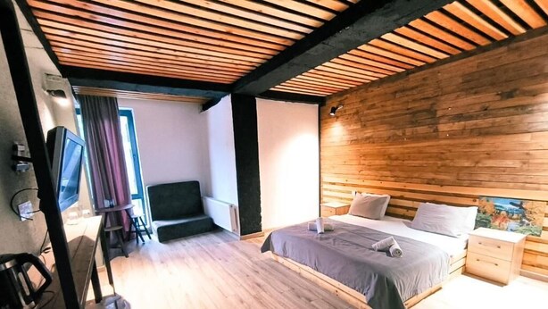 Quarto com teto de madeira, uma cama com almofadas, mesa de cabeceira e televisão.