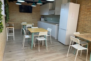 Uma cozinha compacta com armários brancos, uma geladeira branca e uma mesa de jantar de madeira com cadeiras brancas.
